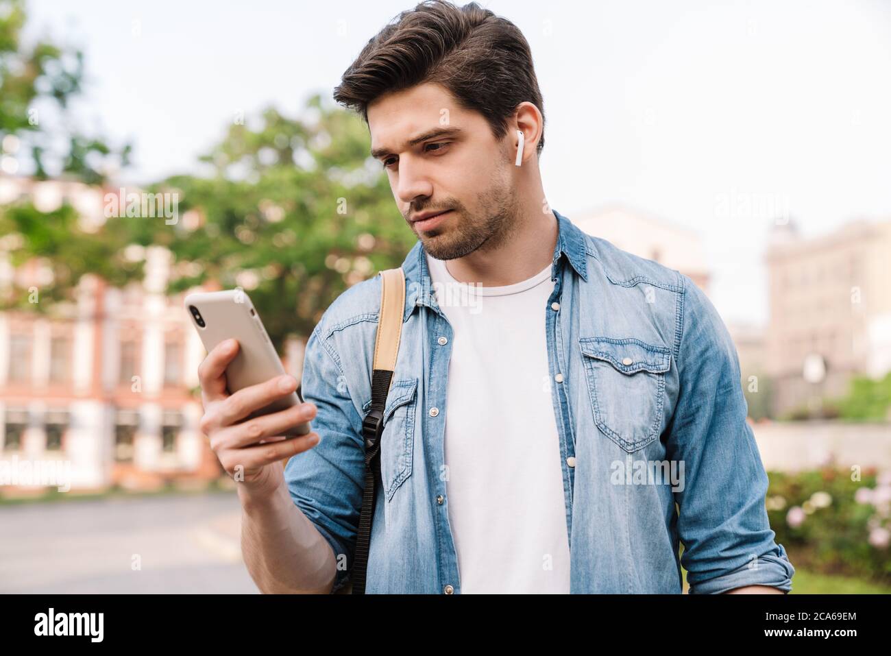 Photo of focused man with wireless earphone using cellphone while ...
