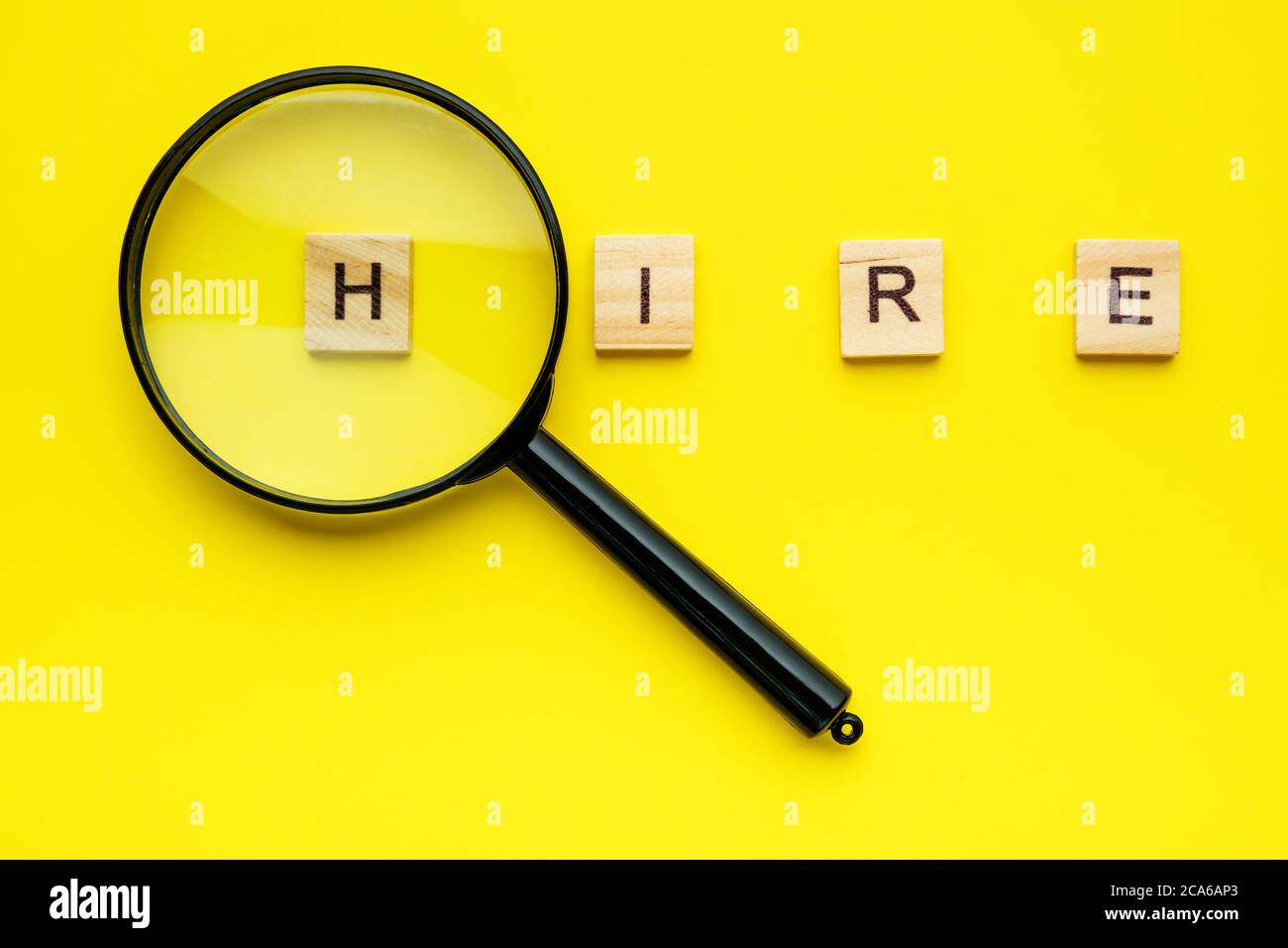 wooden letters blocks with word hire and magnifier on yellow background ...
