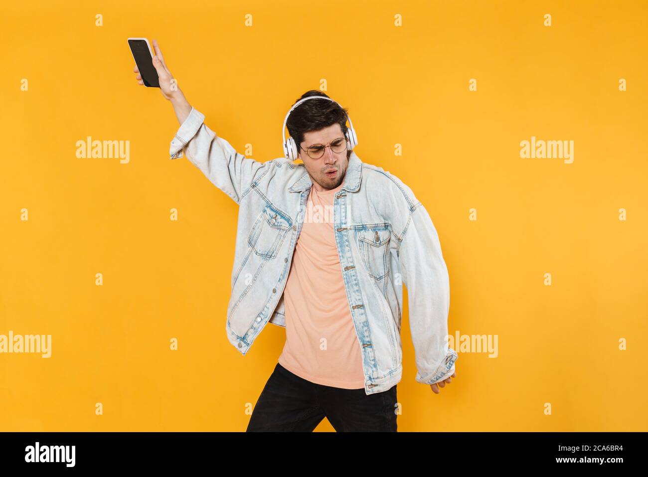 Photo of ecstatic young man using mobile phone and headphones while ...