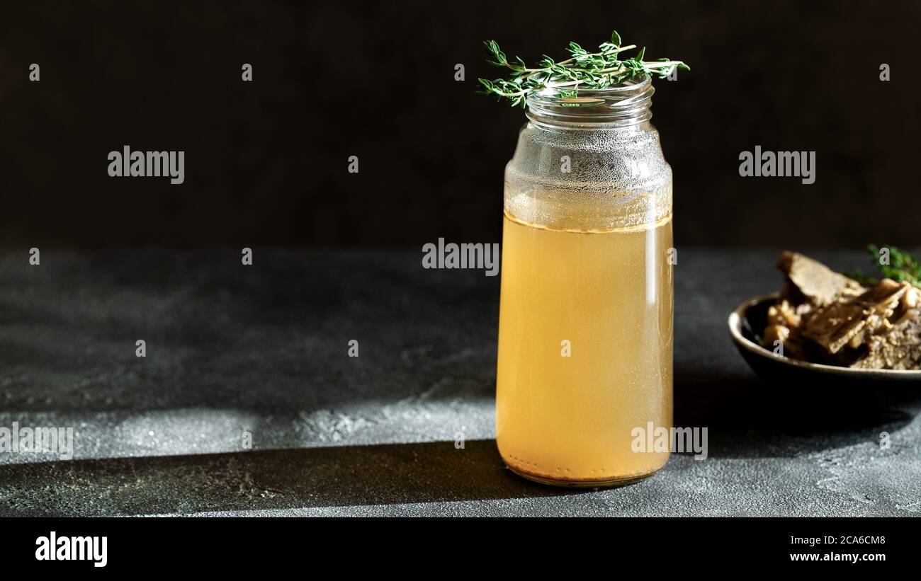 Fresh vegetable bone broth in glass jar with herb on dark gray ...