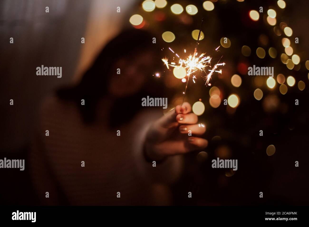 Happy woman holding firework at christmas tree with golden lights ...