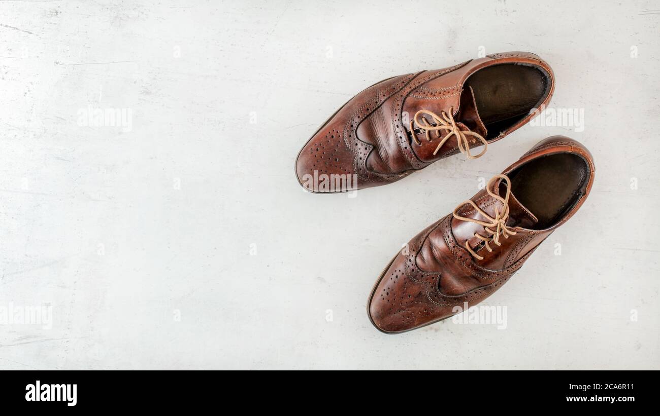 Overhead shot, pair of old worn brown shoes on white board, wide banner ...