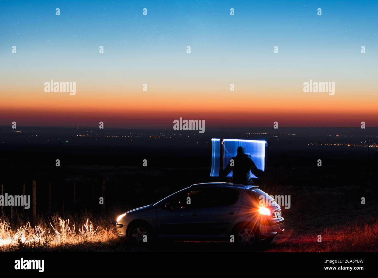 young man sitting on car with a lightpaintin light beam in his hands a ...