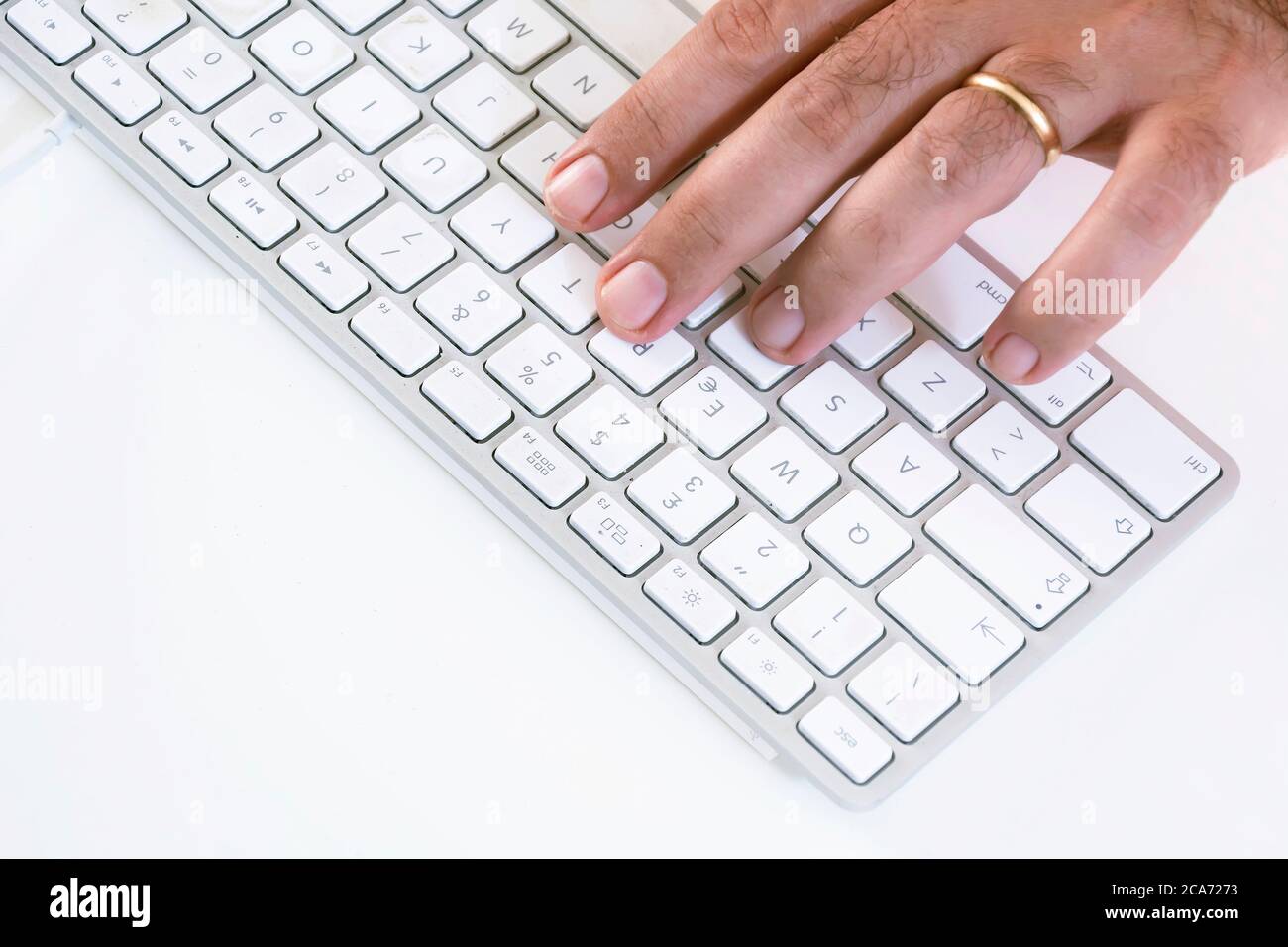 male hand typing on a white keyboard on a white table. White background ...