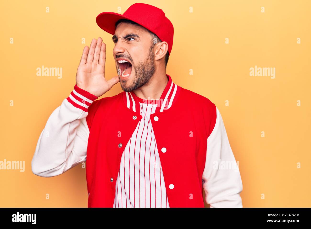 Handsome sporty man with beard wearing baseball jacket and cap over ...