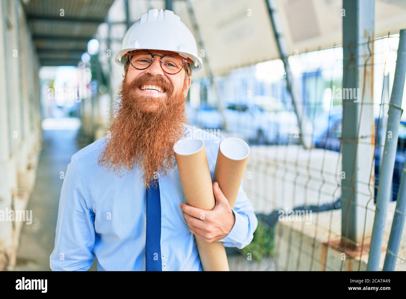 Young redhead architect man with long beard wearing hardhat smiling ...