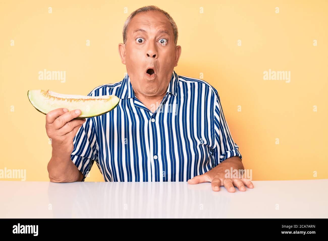 Senior handsome man with gray hair holding fresh melon sitting on the ...
