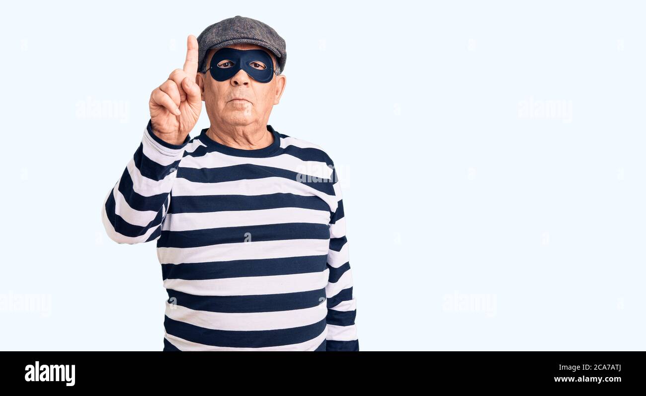 Senior handsome man wearing burglar mask and t-shirt pointing with ...