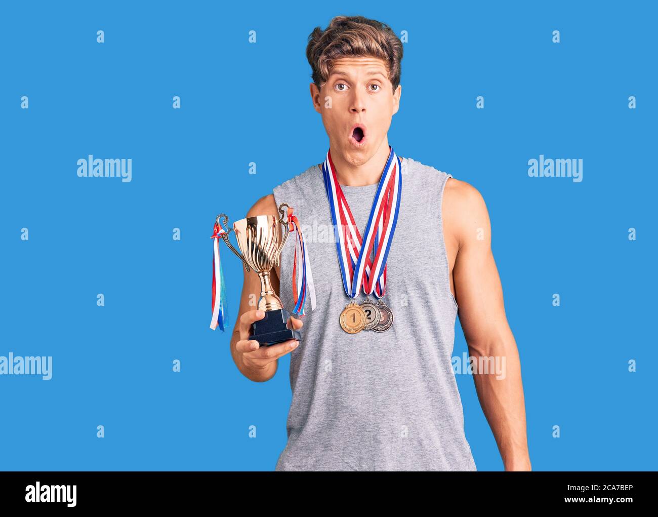 Young handsome man holding champion trophy wearing medals scared and ...