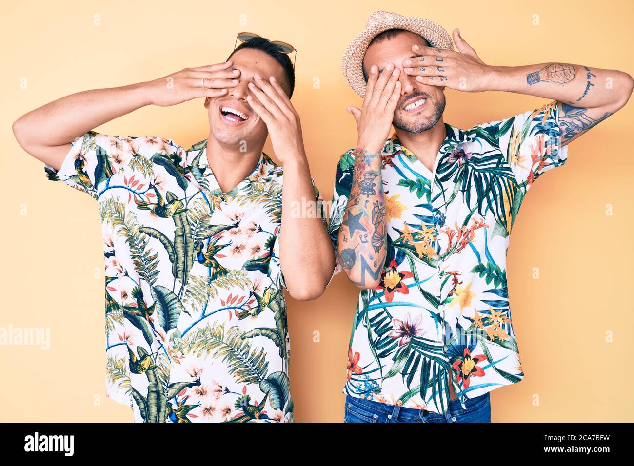 Young gay couple of two men wearing summer hat and hawaiian shirt ...