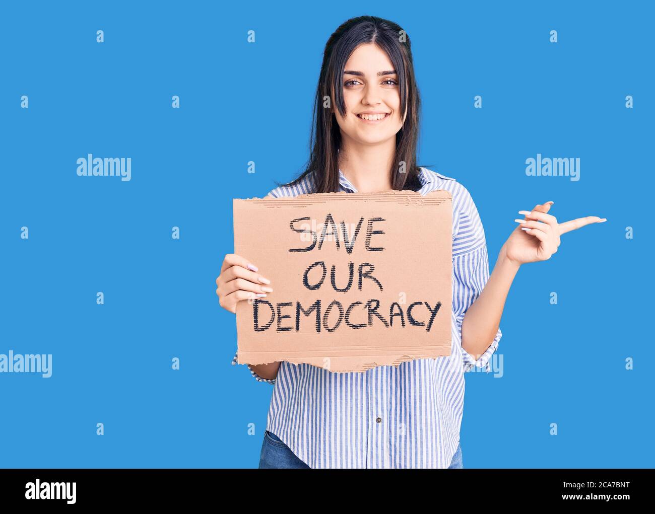 Young beautiful girl holding save our democracy cardboard banner ...