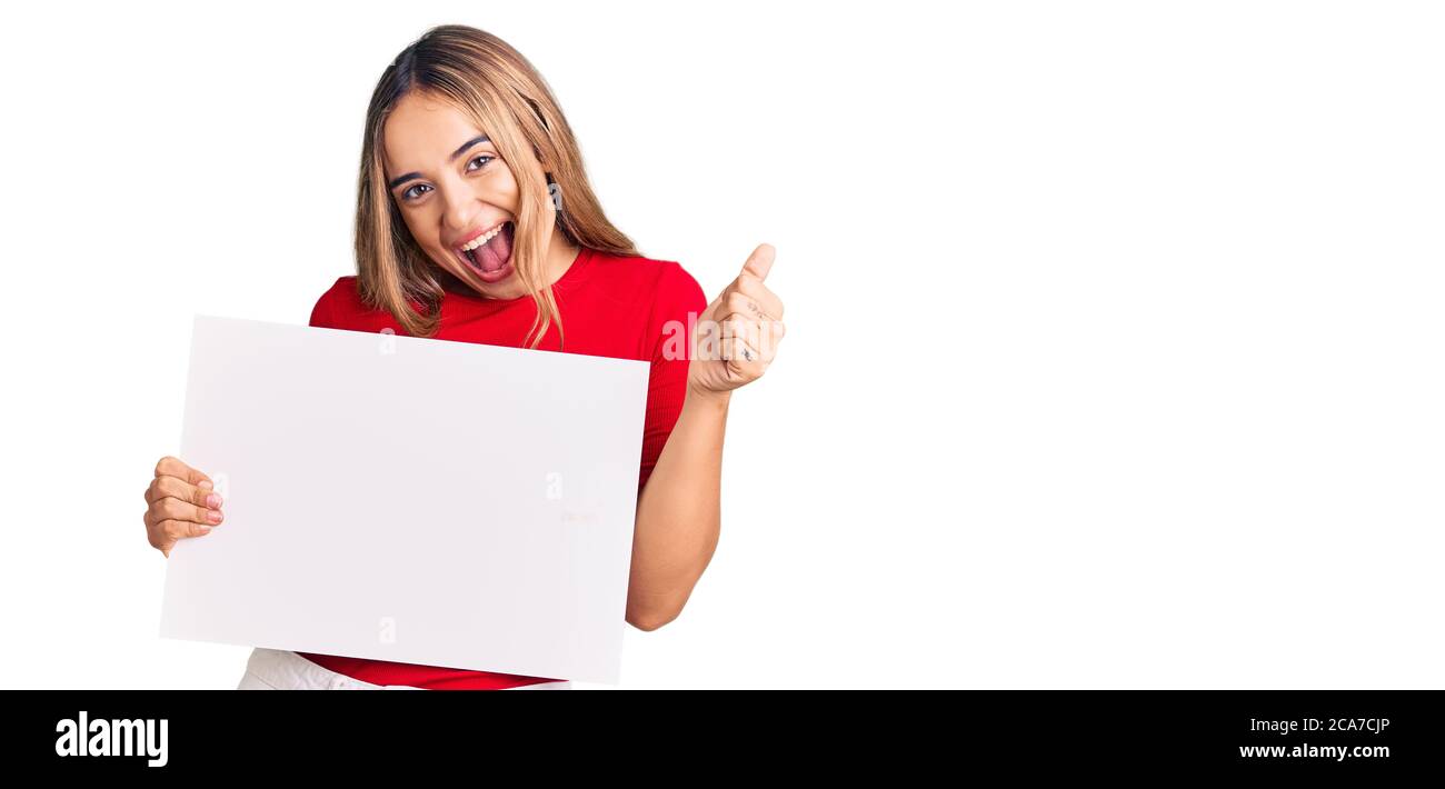 Young beautiful blonde woman holding blank empty banner screaming proud ...
