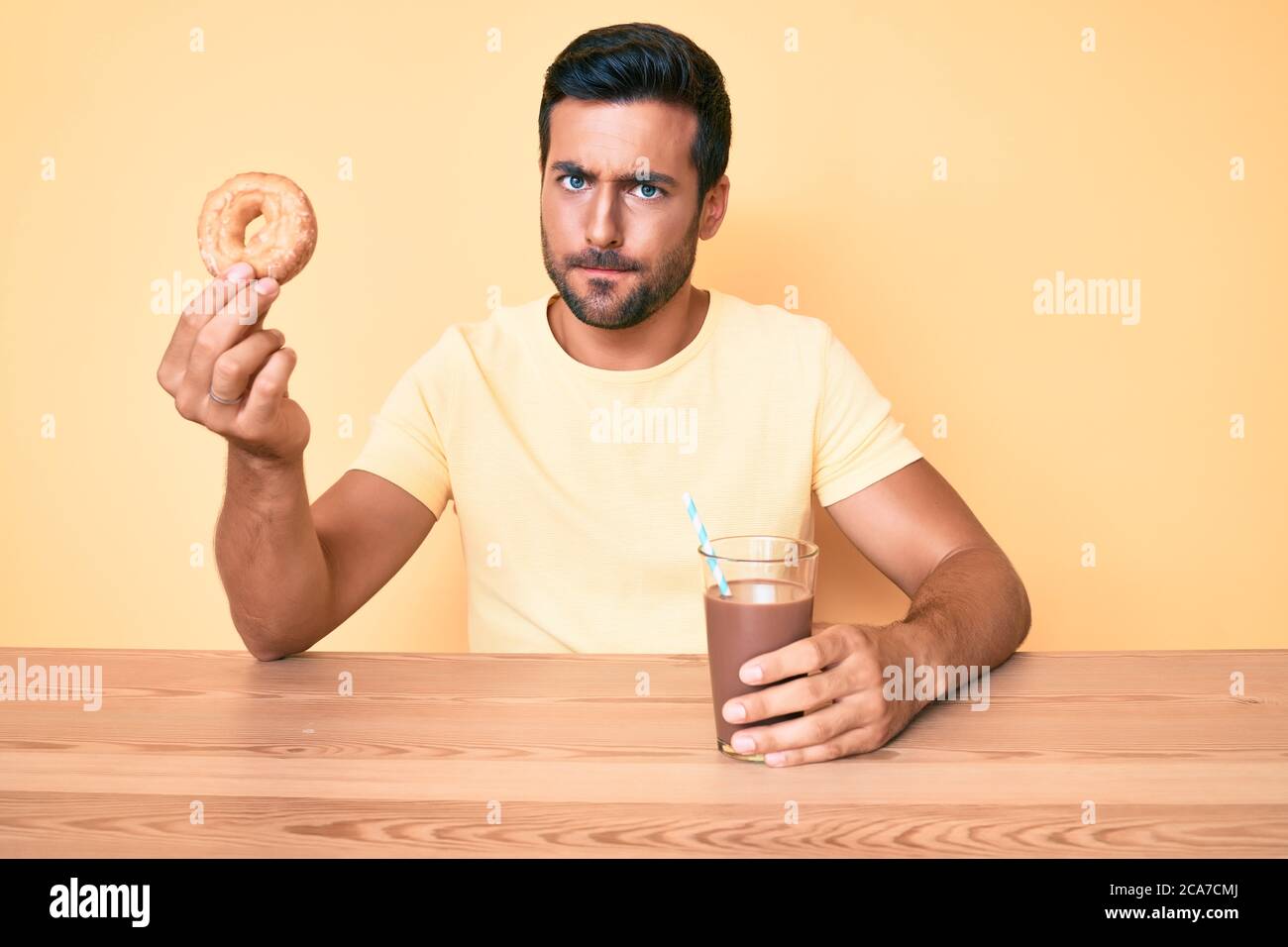 Young hispanic man sitting at the table drinking chocolate beverage ...