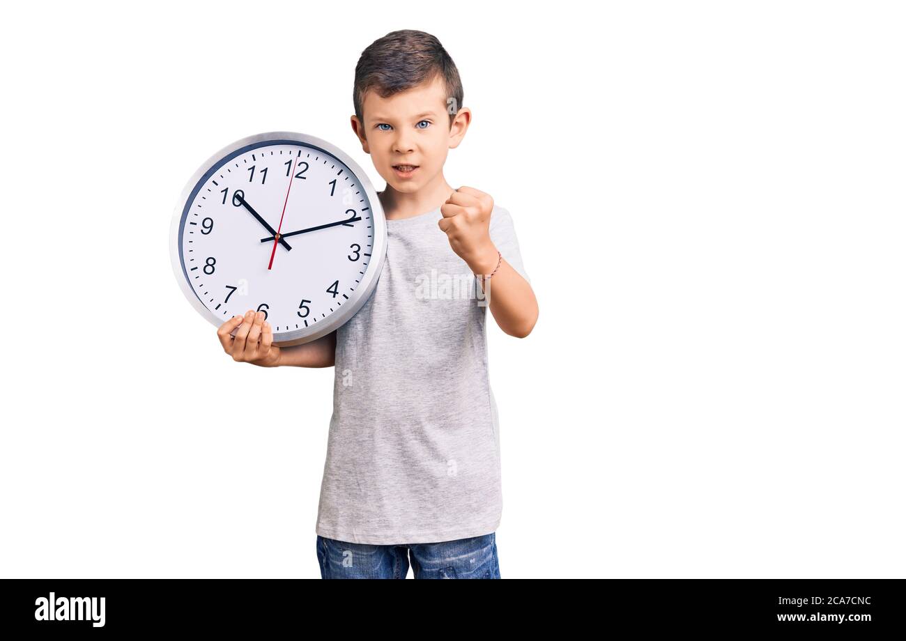 Cute blond kid holding big clock annoyed and frustrated shouting with ...