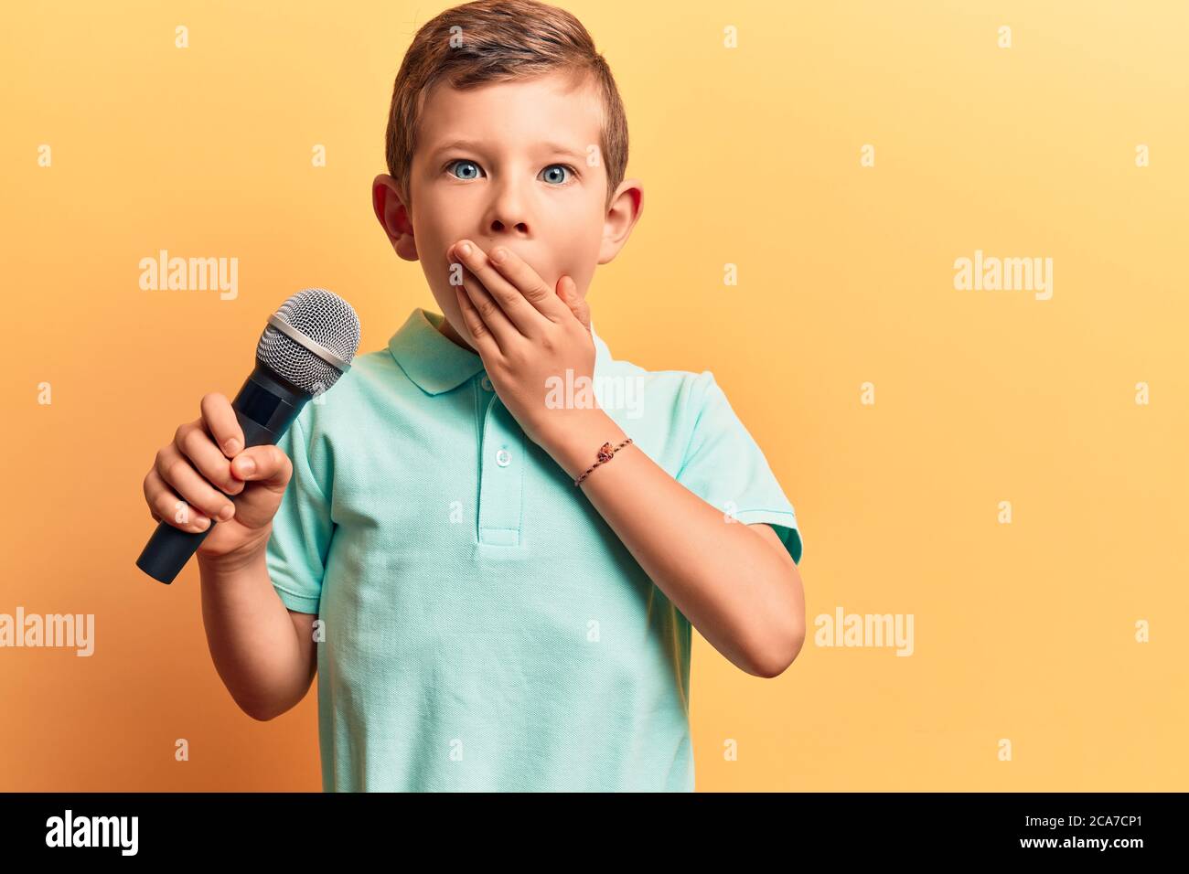 Cute blond kid singing song using microphone covering mouth with hand ...