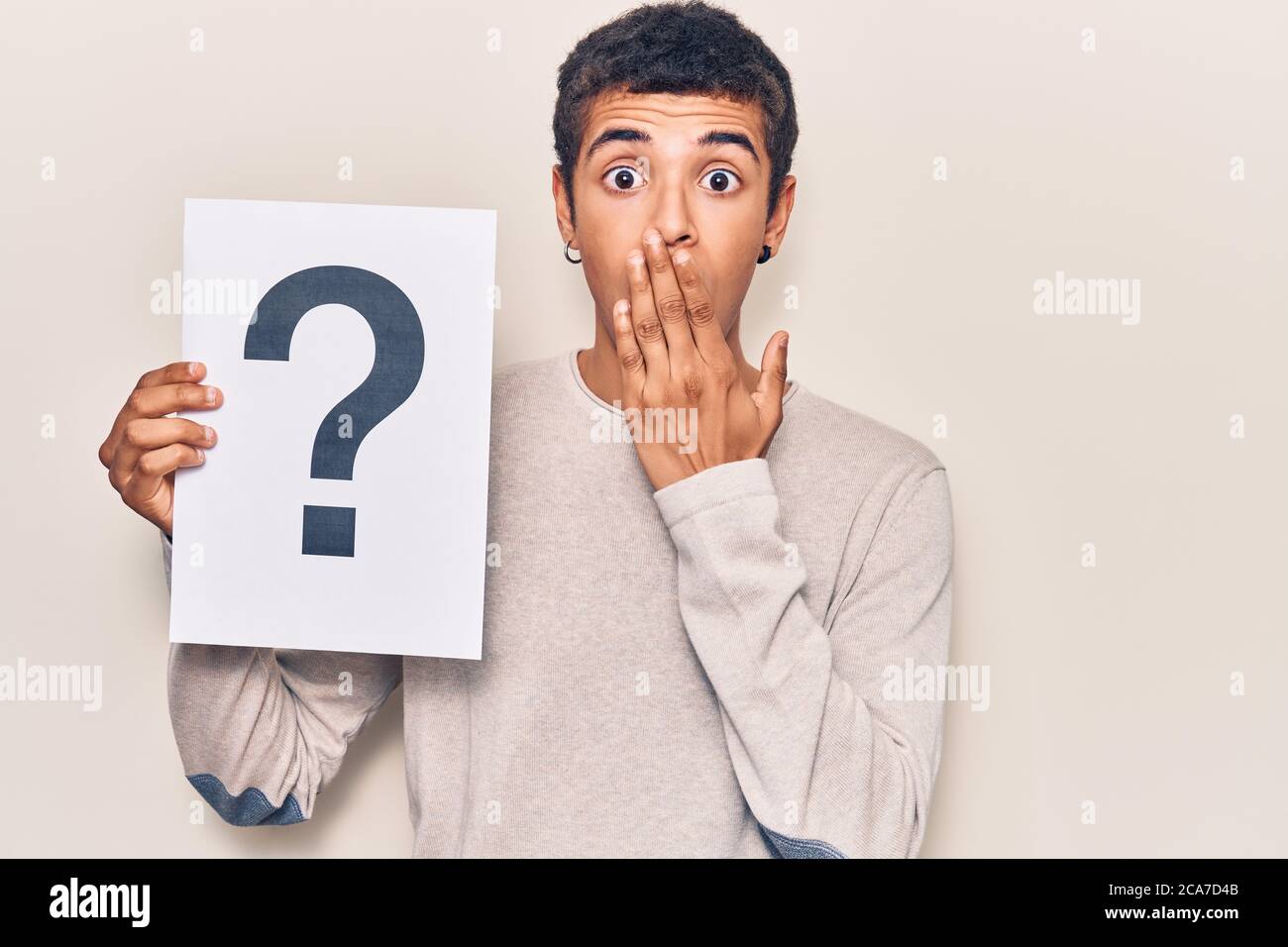 Young african amercian man holding question mark covering mouth with ...