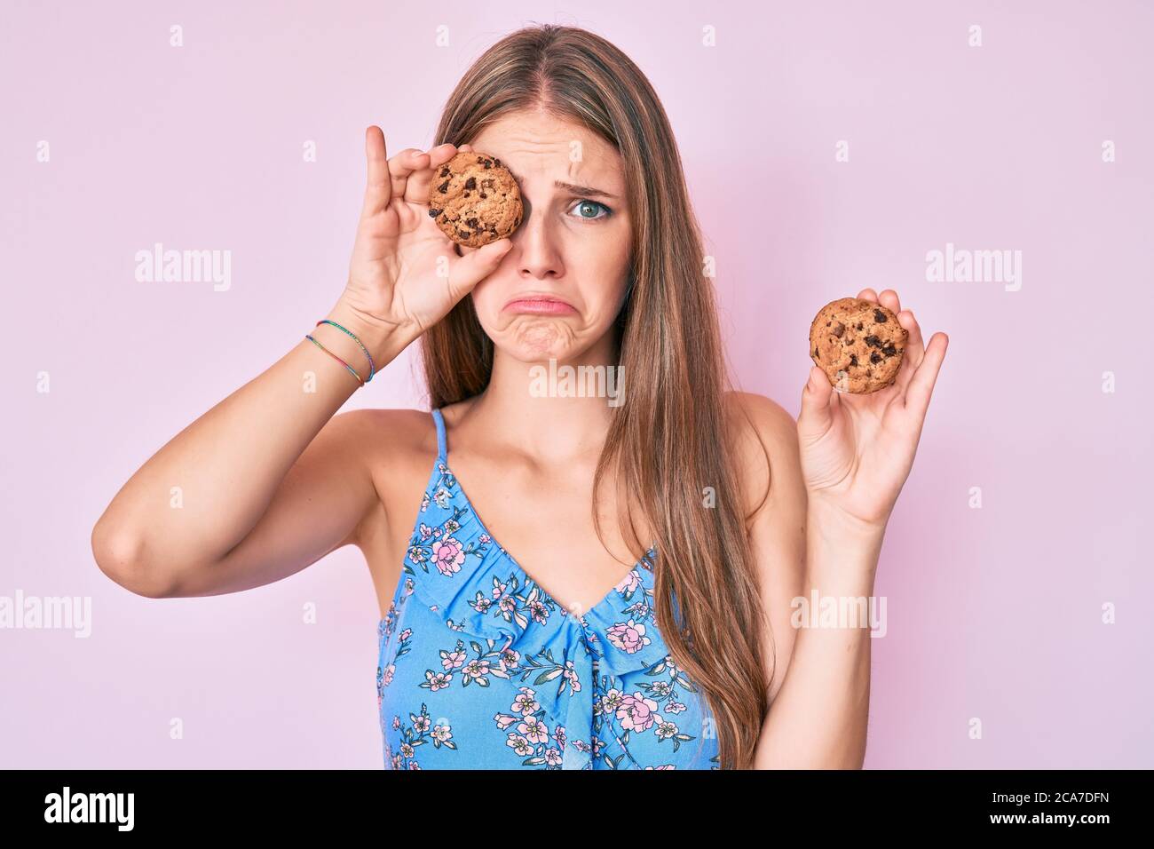 Young blonde girl holding cookie depressed and worry for distress ...