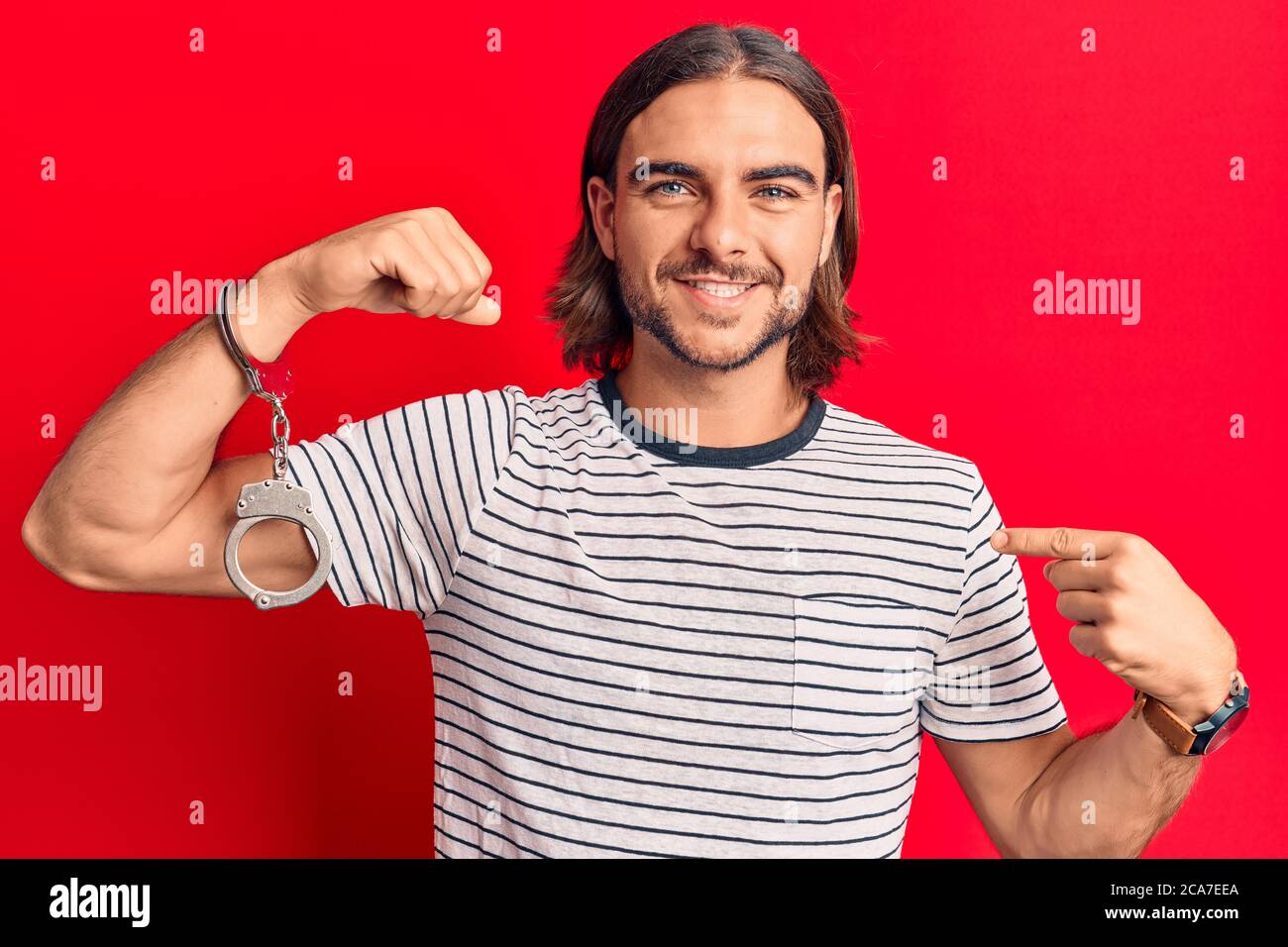 Young handsome man wearing prisoner handcuffs pointing finger to one ...