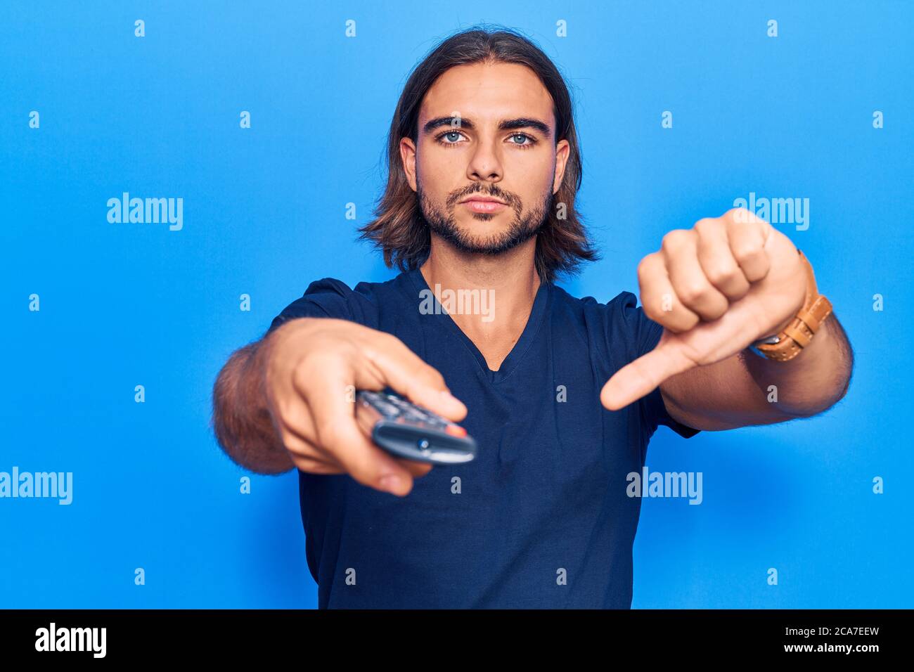 Young handsome man holding television remote control with angry face ...