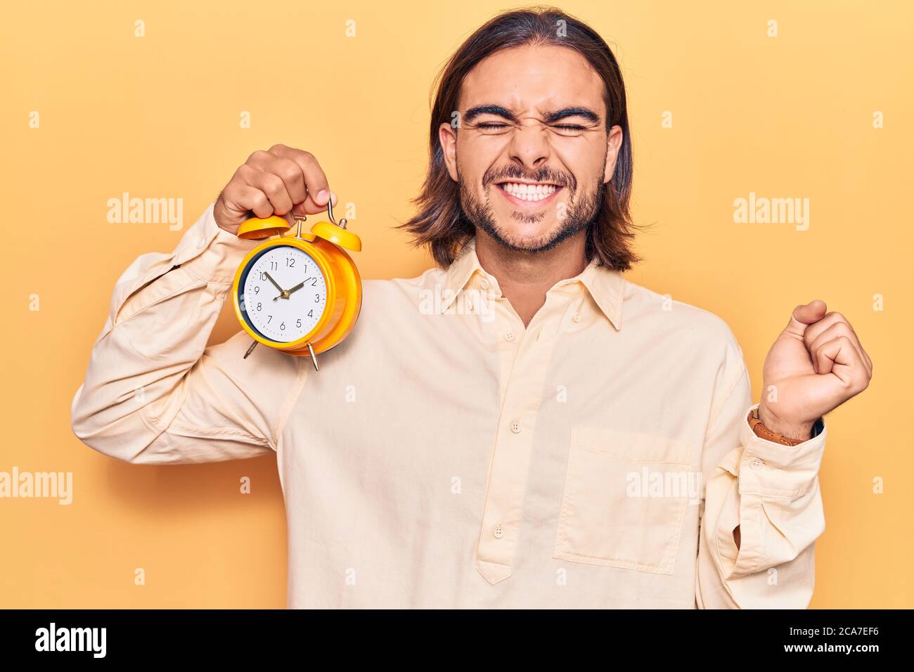 Young handsome man holding alarm clock screaming proud, celebrating ...