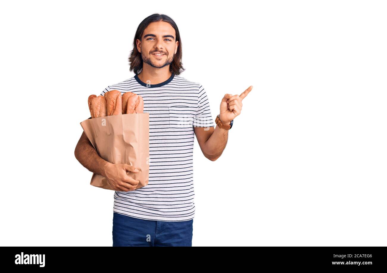 Young handsome man holding paper bag with bread smiling happy pointing ...