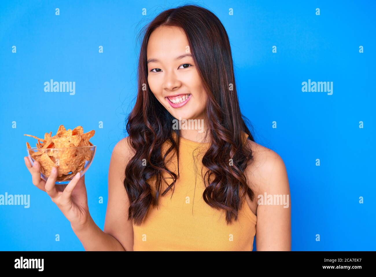 Young beautiful chinese girl holding nachos potato chips looking ...