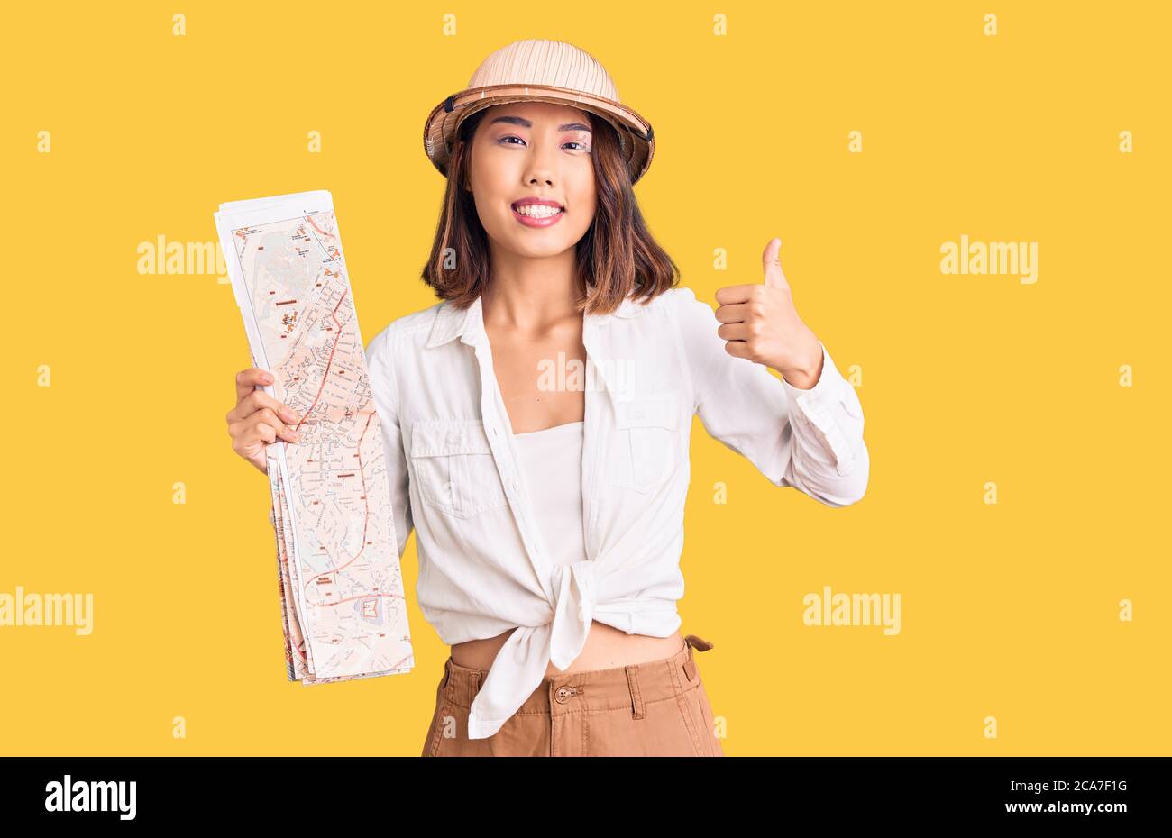 Young beautiful chinese girl wearing explorer hat holding map smiling ...