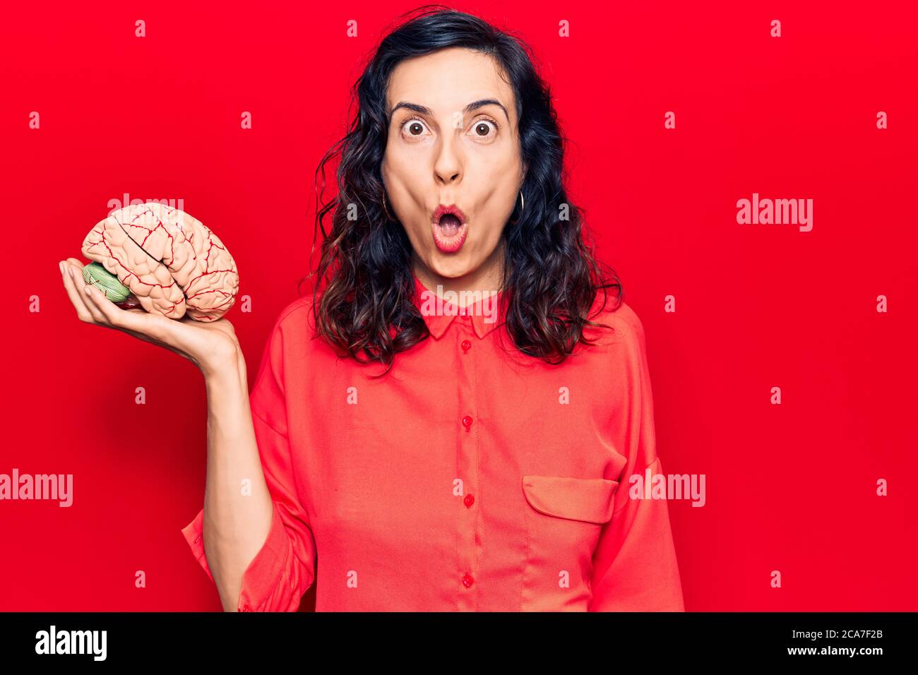 Young beautiful hispanic woman holding brain scared and amazed with ...