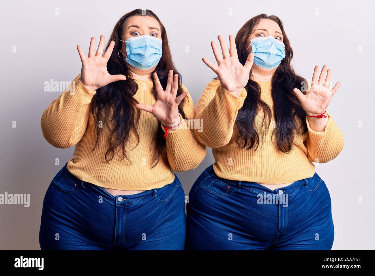 Young plus size twins wearing medical mask afraid and terrified with ...