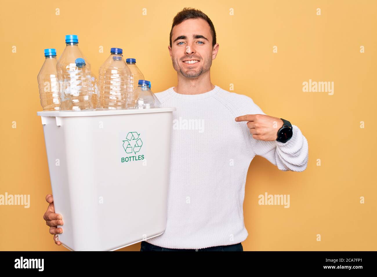 Young handsome man with blue eyes recycling holding wastebasket with ...
