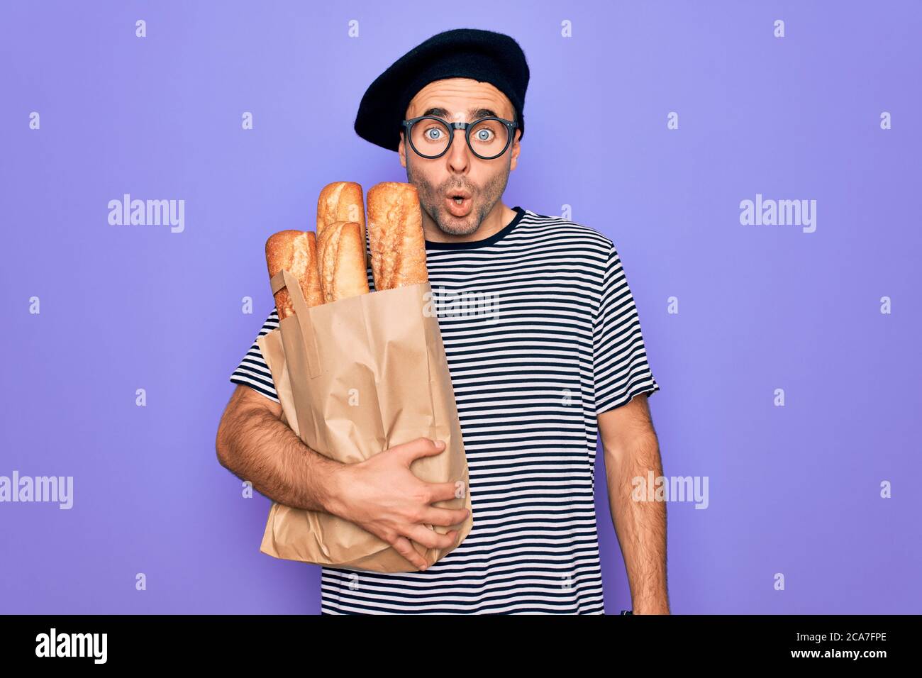 Young handsome baker man with blue eyes wearing french beret holding ...