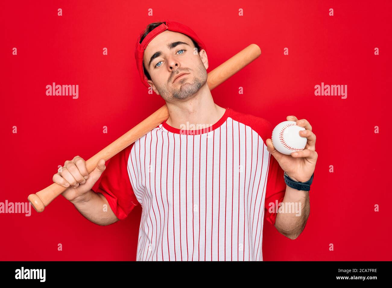 Young handsome sporty man with blue eyes playing baseball wearing cap ...