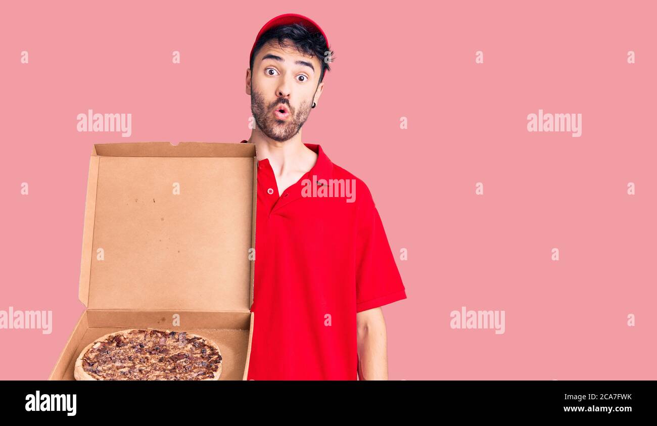 Young hispanic man holding delivery pizza box scared and amazed with ...