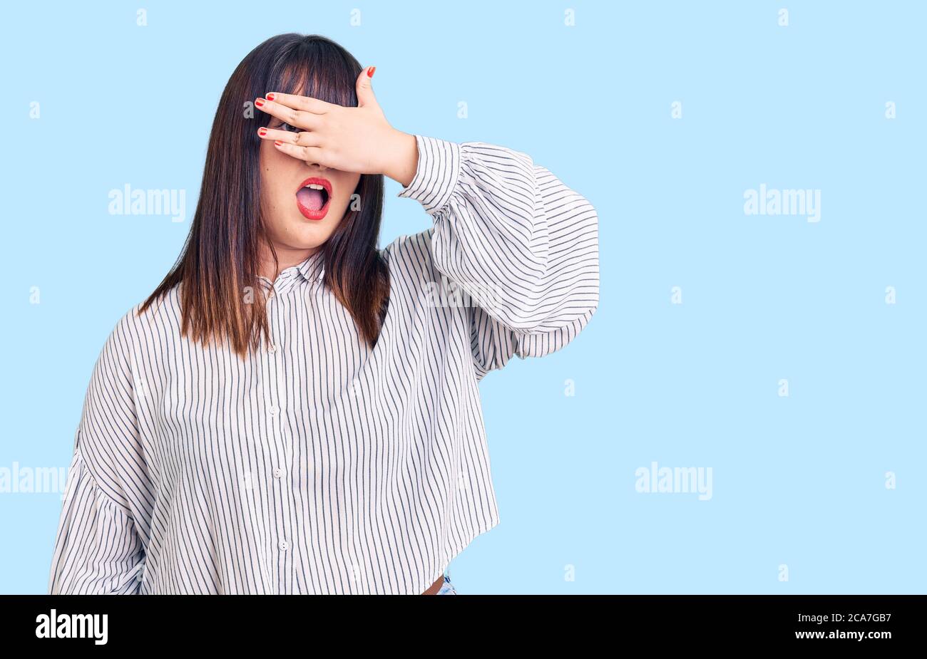 Young plus size woman wearing casual clothes peeking in shock covering ...