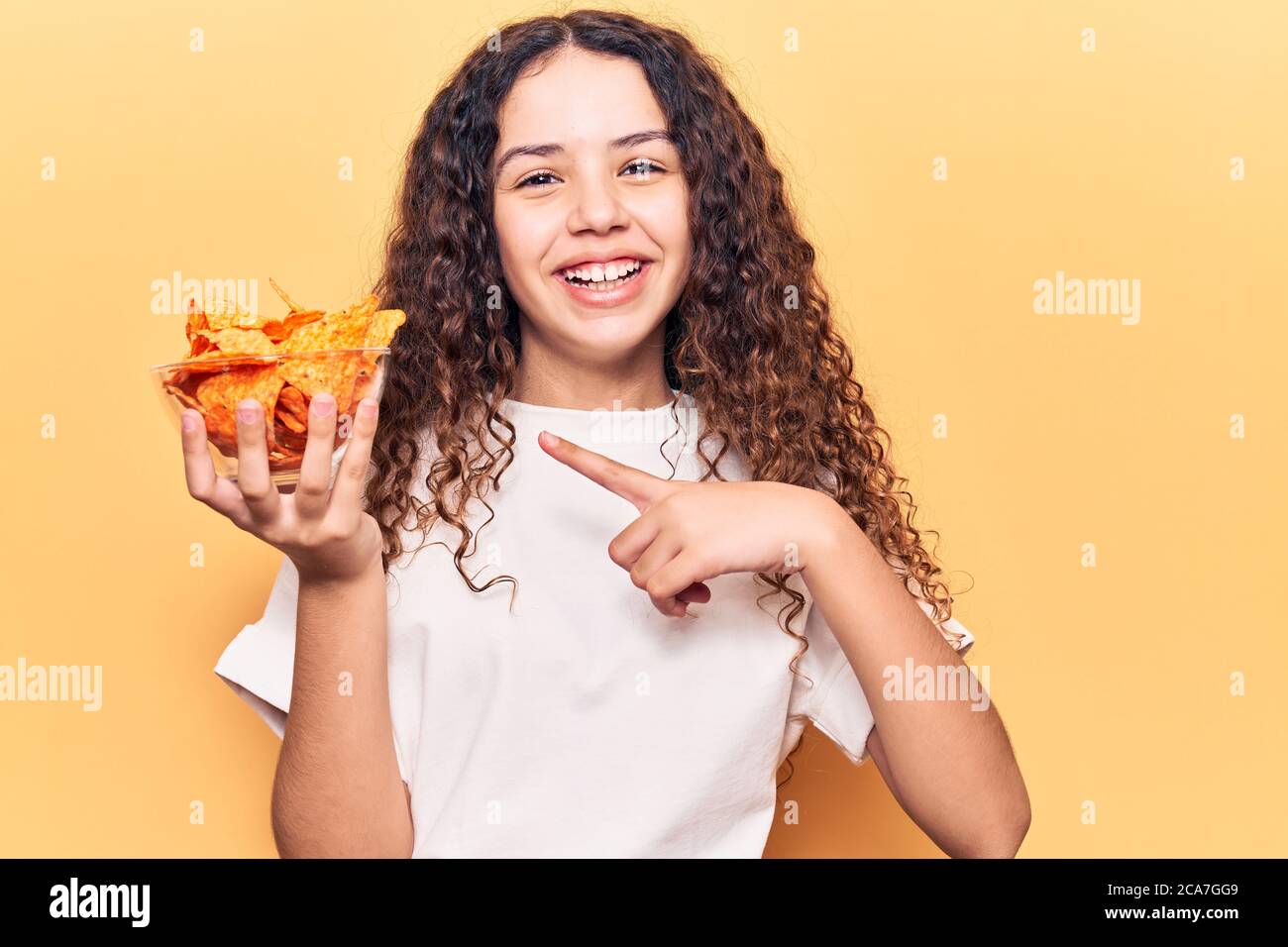 Beautiful kid girl with curly hair holding nachos potato chips smiling ...
