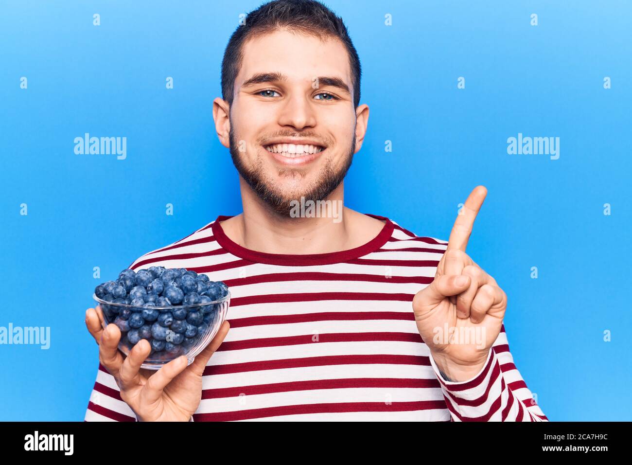 Young handsome man holding bowl with blueberries smiling with an idea ...