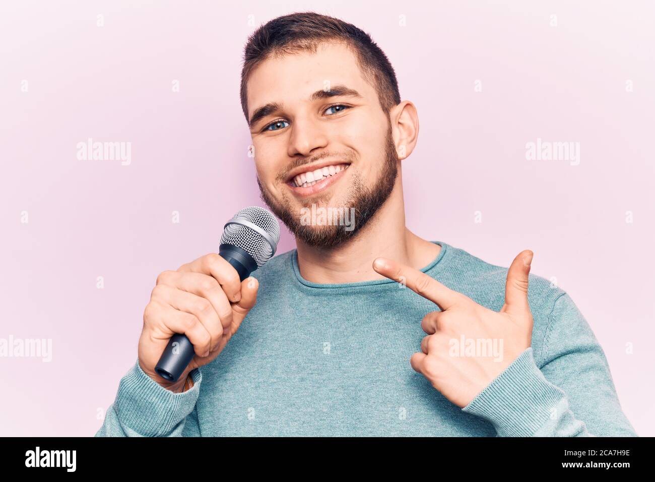 Young handsome man singing song using microphone smiling happy pointing with hand and finger ...