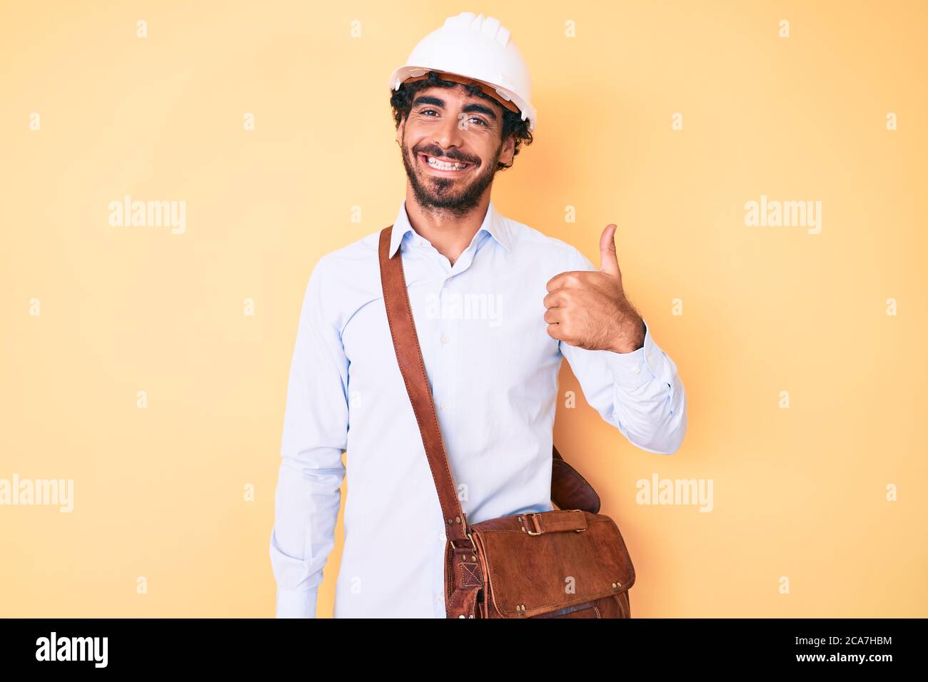 Handsome young man with curly hair and bear wearing architect hardhat ...