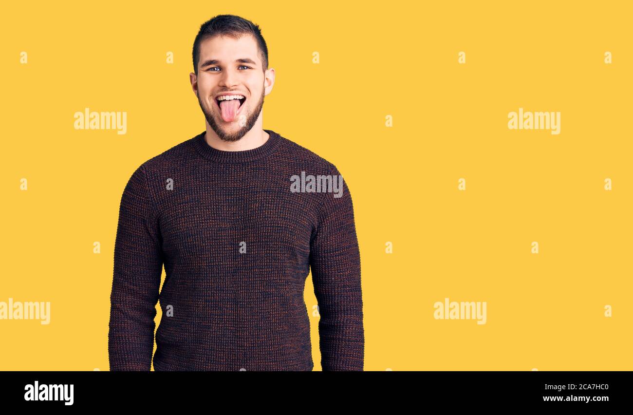 Young handsome man wearing casual sweater sticking tongue out happy ...