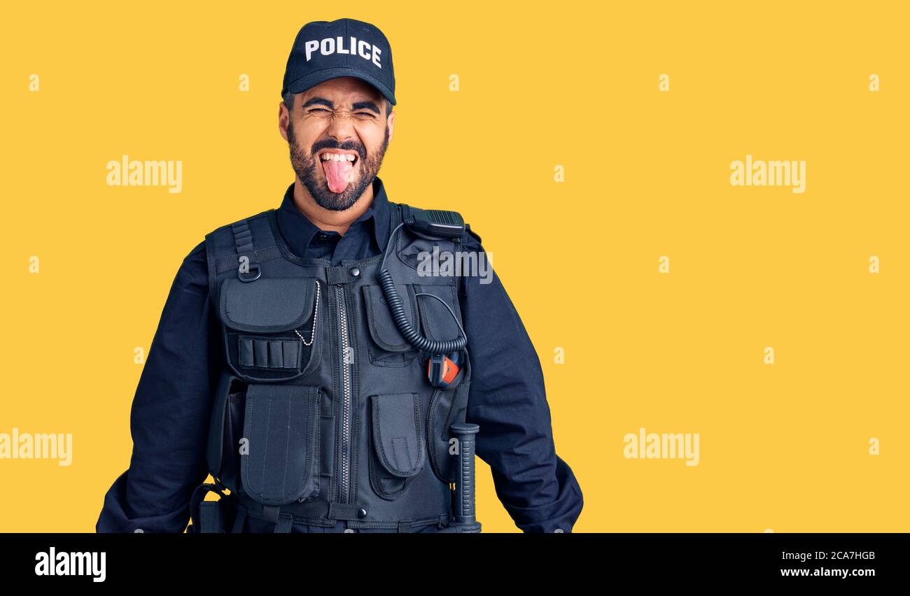 Young hispanic man wearing police uniform sticking tongue out happy ...