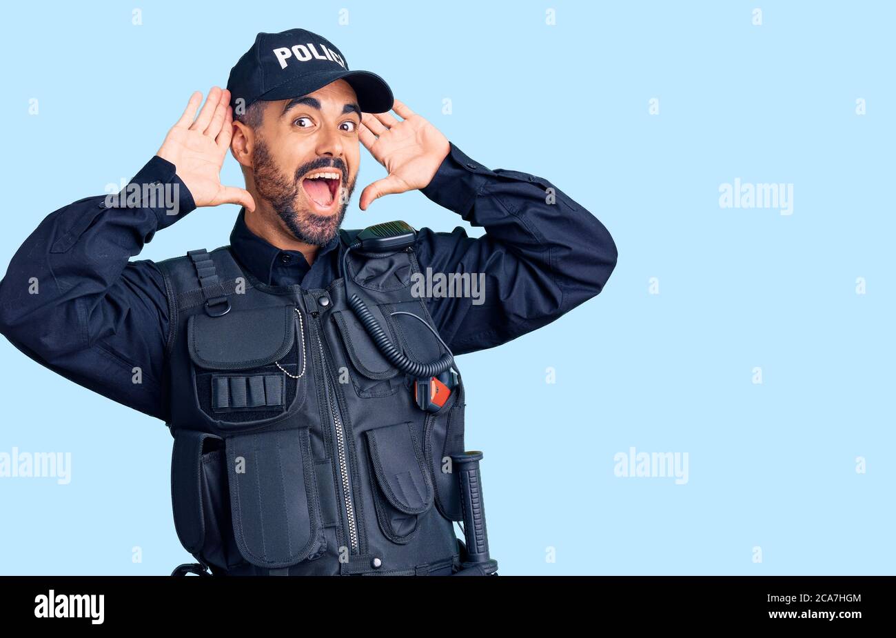 Young hispanic man wearing police uniform smiling cheerful playing peek ...