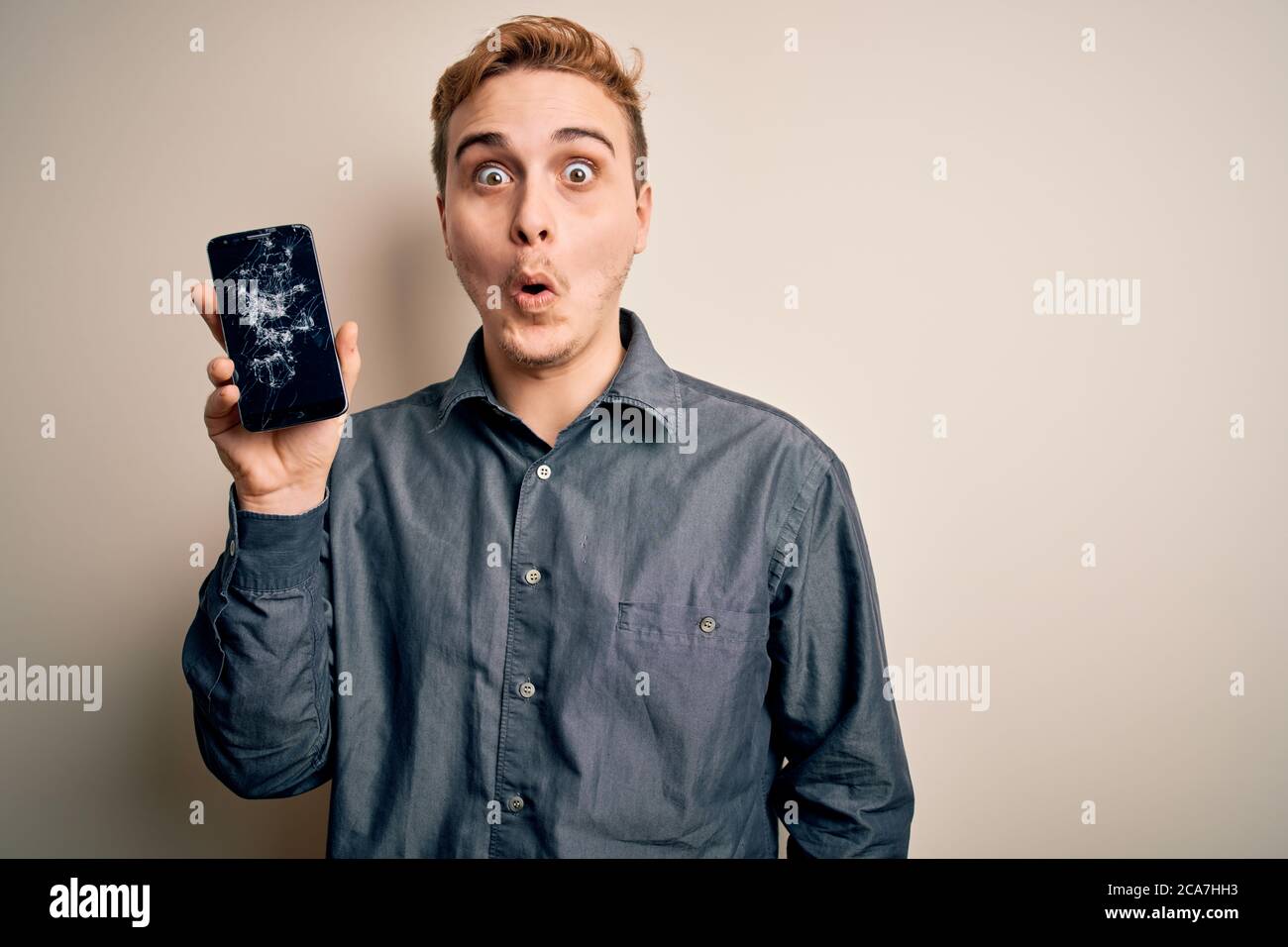 Young handsome redhead man holding broken smartphone showing cracked ...