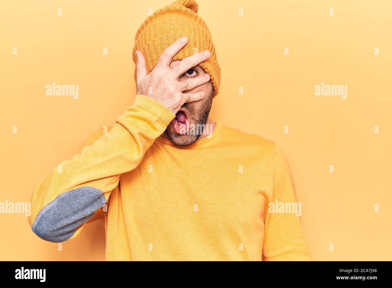 Young handsome bald man wearing sweater and wool cap peeking in shock ...