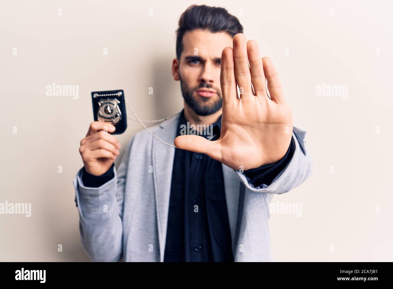 Young handsome man with beard holding police badge with open hand doing ...