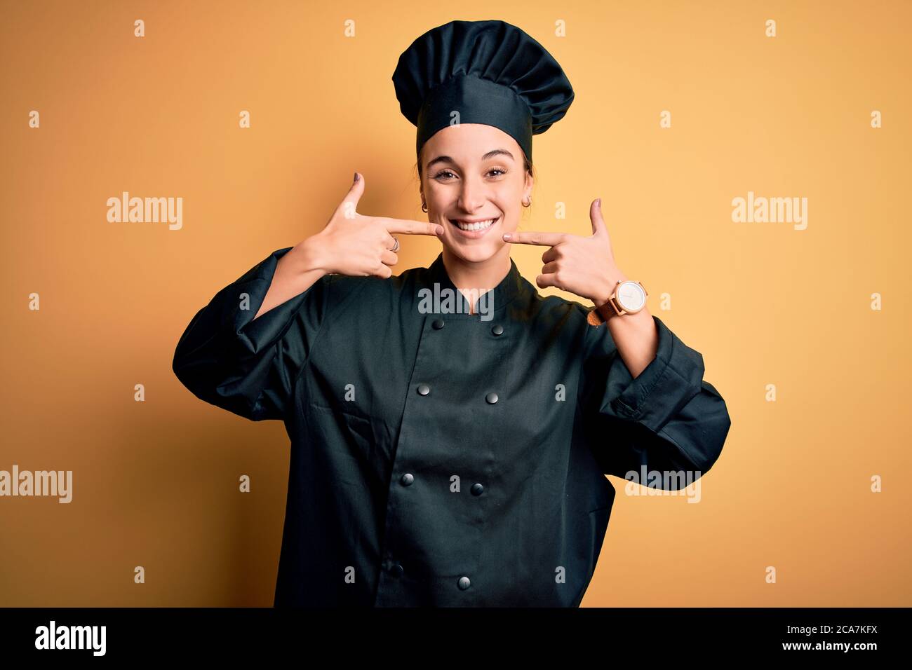 Young beautiful chef woman wearing cooker uniform and hat standing over ...