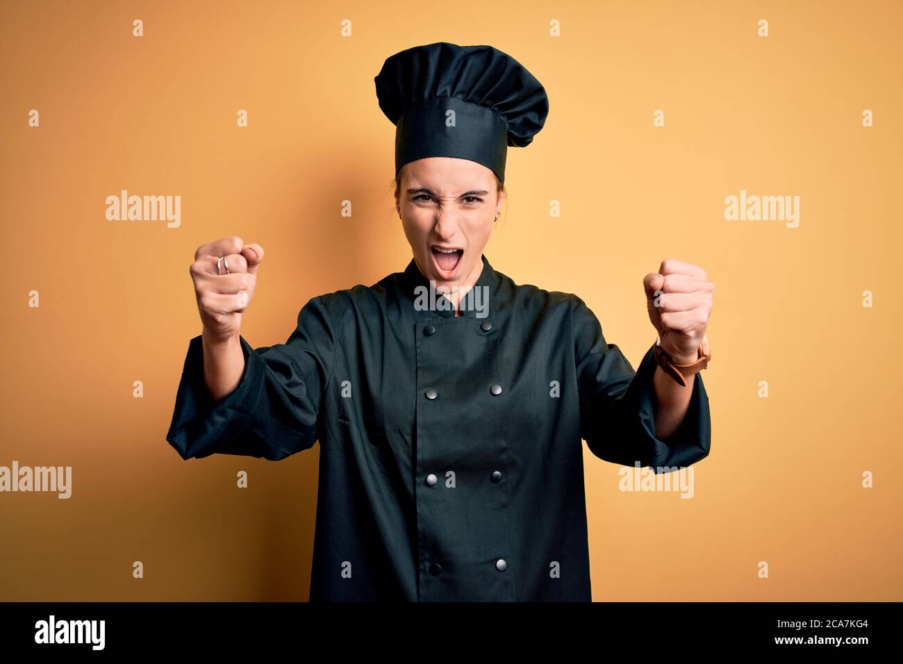 Young beautiful chef woman wearing cooker uniform and hat standing over ...