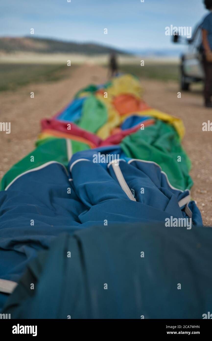 Deflated hot air balloon on dusty road. People and mountains visible in ...