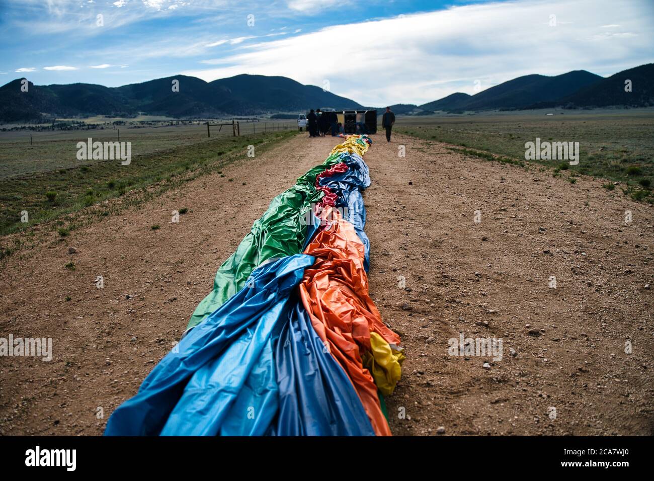 Deflated hot air balloon on dusty road. People and mountains visible in ...