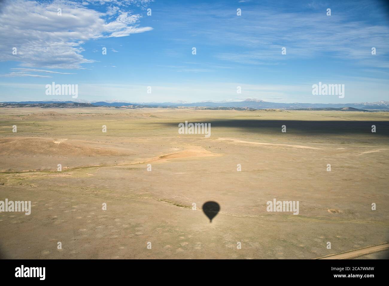 Shadow of hot air balloon looking over vast plane with rocky mountains ...