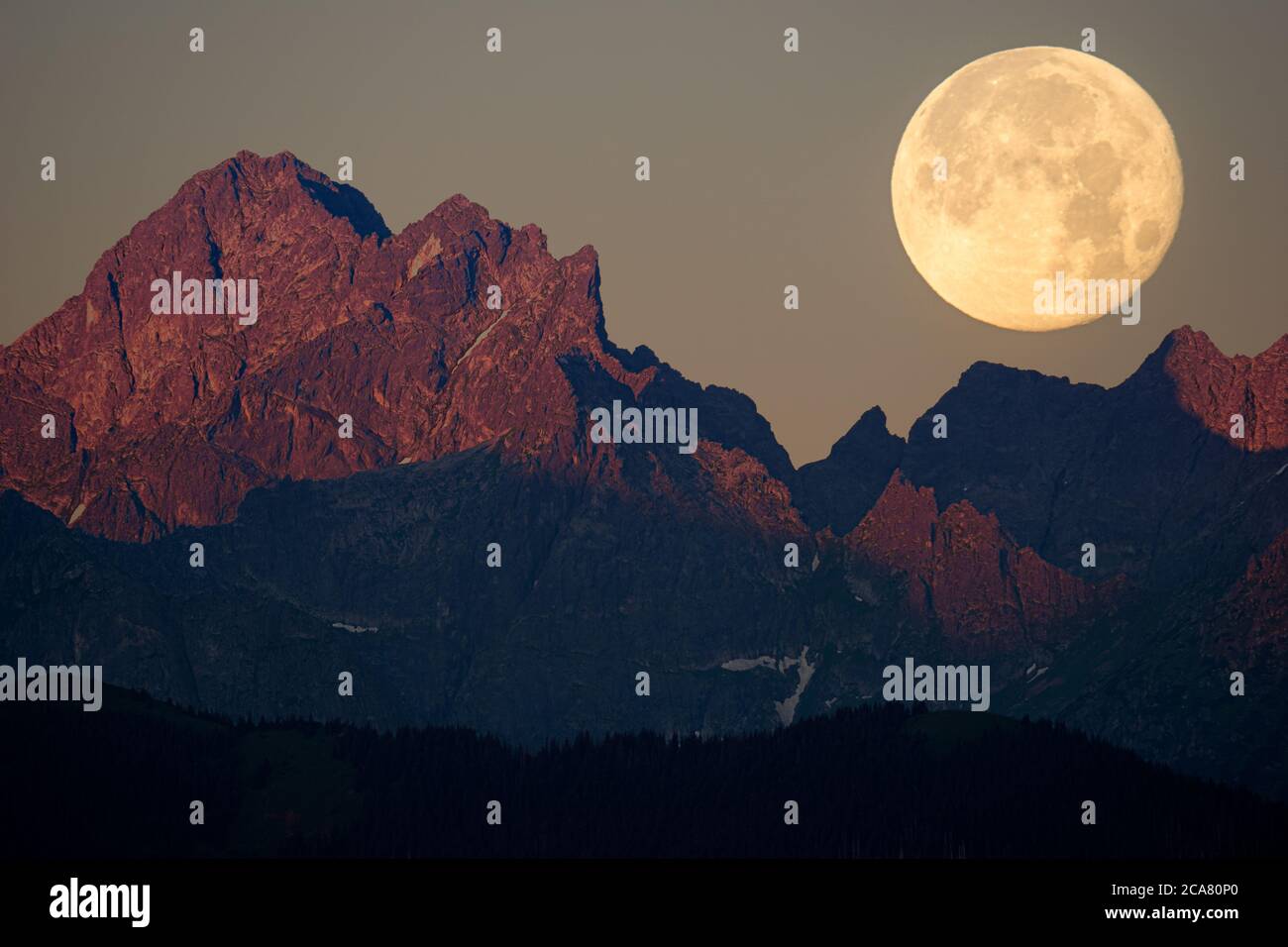 full moon setting behind the top of the mountain lit by the sun just ...